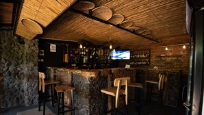 Uma área de bar com paredes de pedra, balcão de madeira e várias cadeiras de madeira.