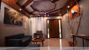 Uma sala de estar moderna com sofá, poltrona e mesa de centro. Há um quadro na parede e uma porta de madeira.
