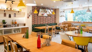 Um café moderno com mesas e cadeiras de madeira, luminárias pendentes amarelas e uma parede de tijolos com espelho.