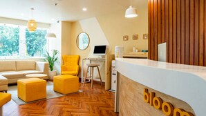 Uma área de recepção moderna com um balcão de madeira, uma poltrona amarela e piso de madeira em padrão herringbone.