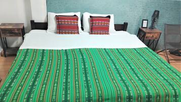 Uma cama com colcha verde estampada, duas almofadas com listras coloridas e cabeceira verde-água.