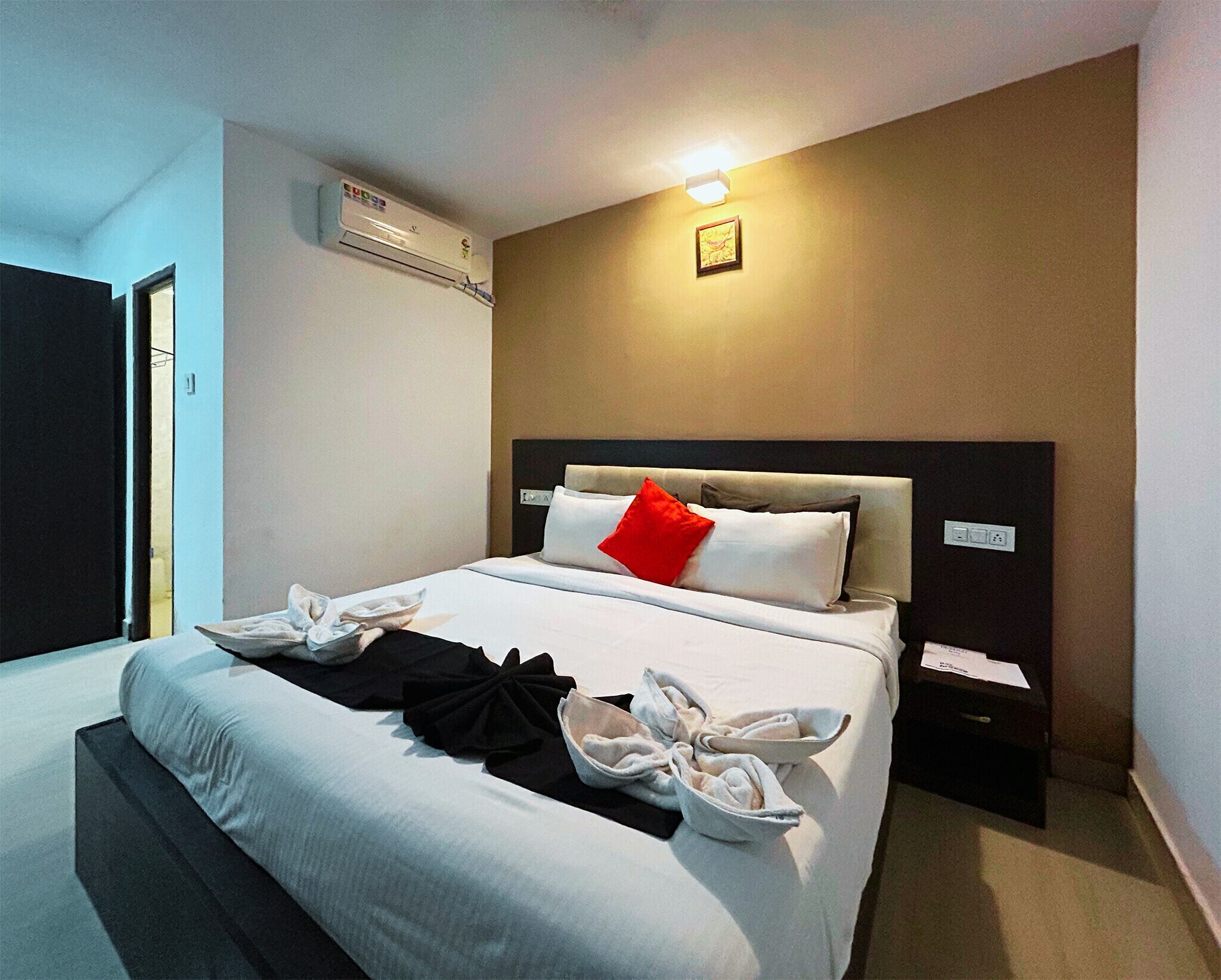 Quarto de hotel com cama, mesa de cabeceira, ar condicionado e luminária na parede.
