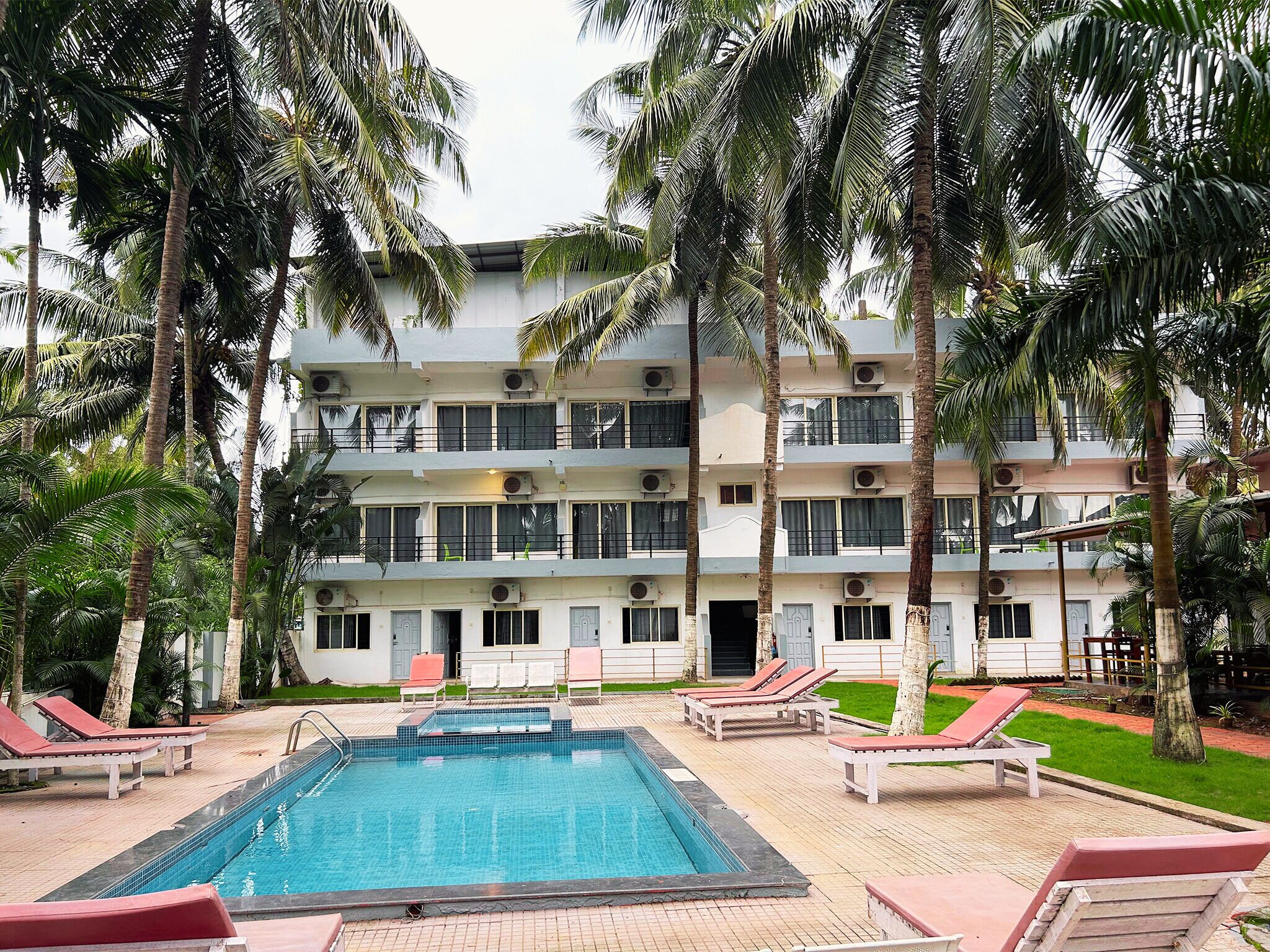 Um hotel com piscina, rodeado por palmeiras e espreguiçadeiras.