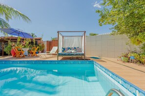 Piscina com fundo de vidro, toldo e cama com almofadas.