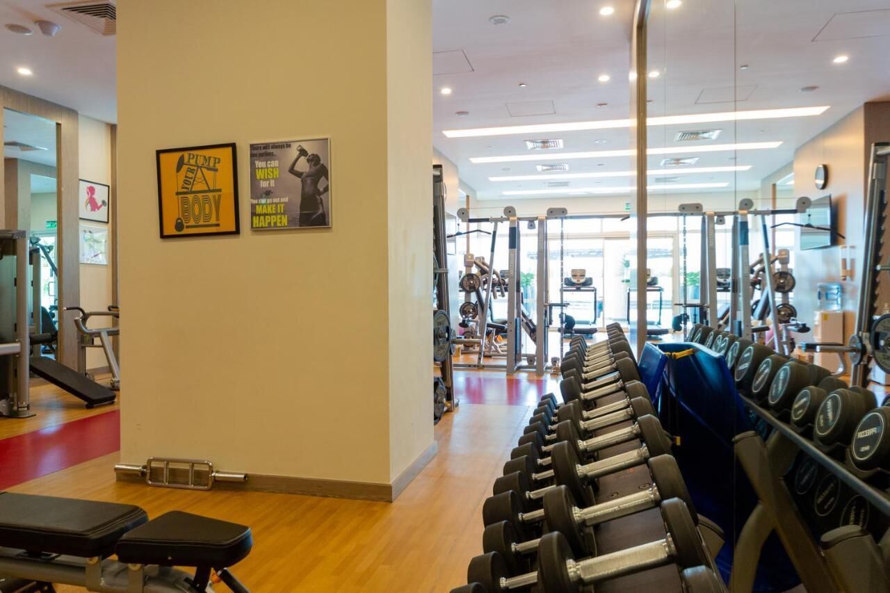 Uma academia com equipamentos de ginástica, incluindo halteres e aparelhos de musculação, e cartazes motivacionais na parede.