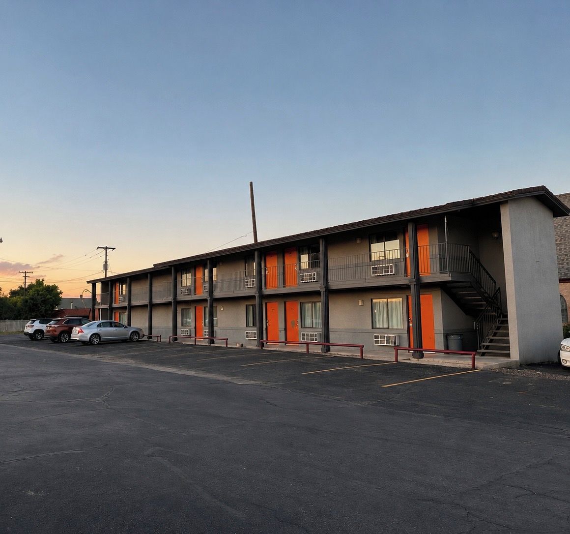 Um motel de vários andares com estacionamento, apresentando uma escadaria central e varandas.