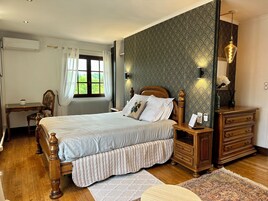 Quarto com cama grande, cômoda de madeira, escrivaninha e janela com cortinas.