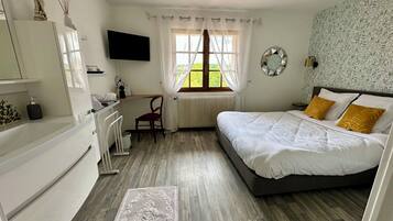 Quarto com cama, escrivaninha, cadeira, televisão e janela com cortinas.