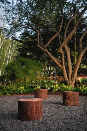 Três vasos de madeira sobre cascalho num jardim, com árvores e folhagem ao fundo.