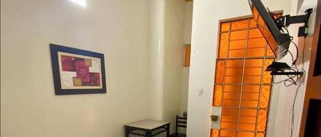 Quarto pequeno e compacto com cama, cadeira, mesa e janela com grade de metal.