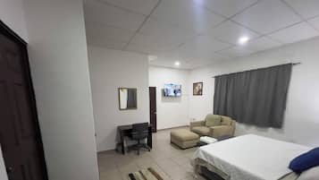 Quarto com cama, escrivaninha, cadeira, sofá e televisão.