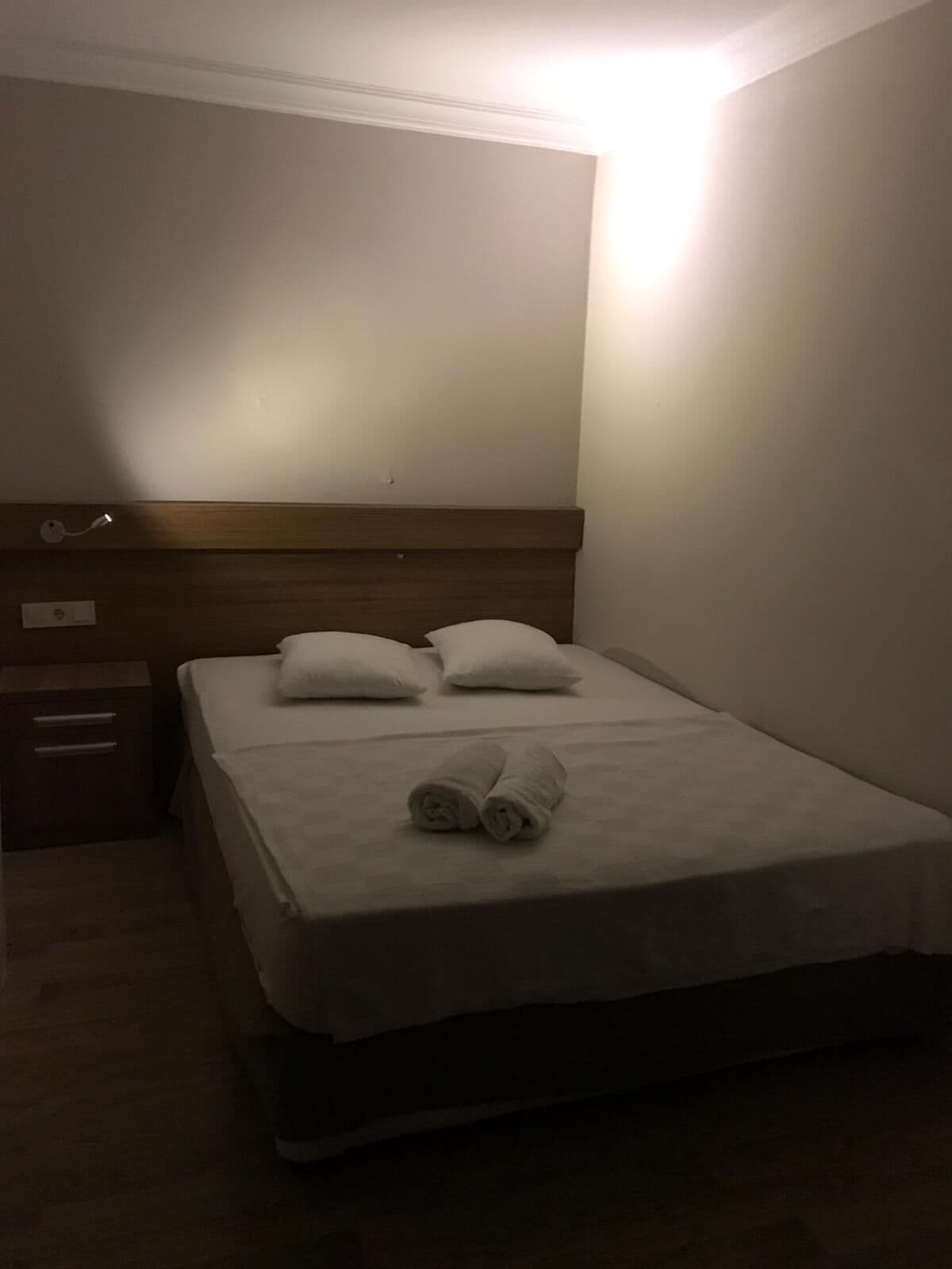 Quarto de hotel com uma cama, duas almofadas, uma mesa de cabeceira e um abajur.
