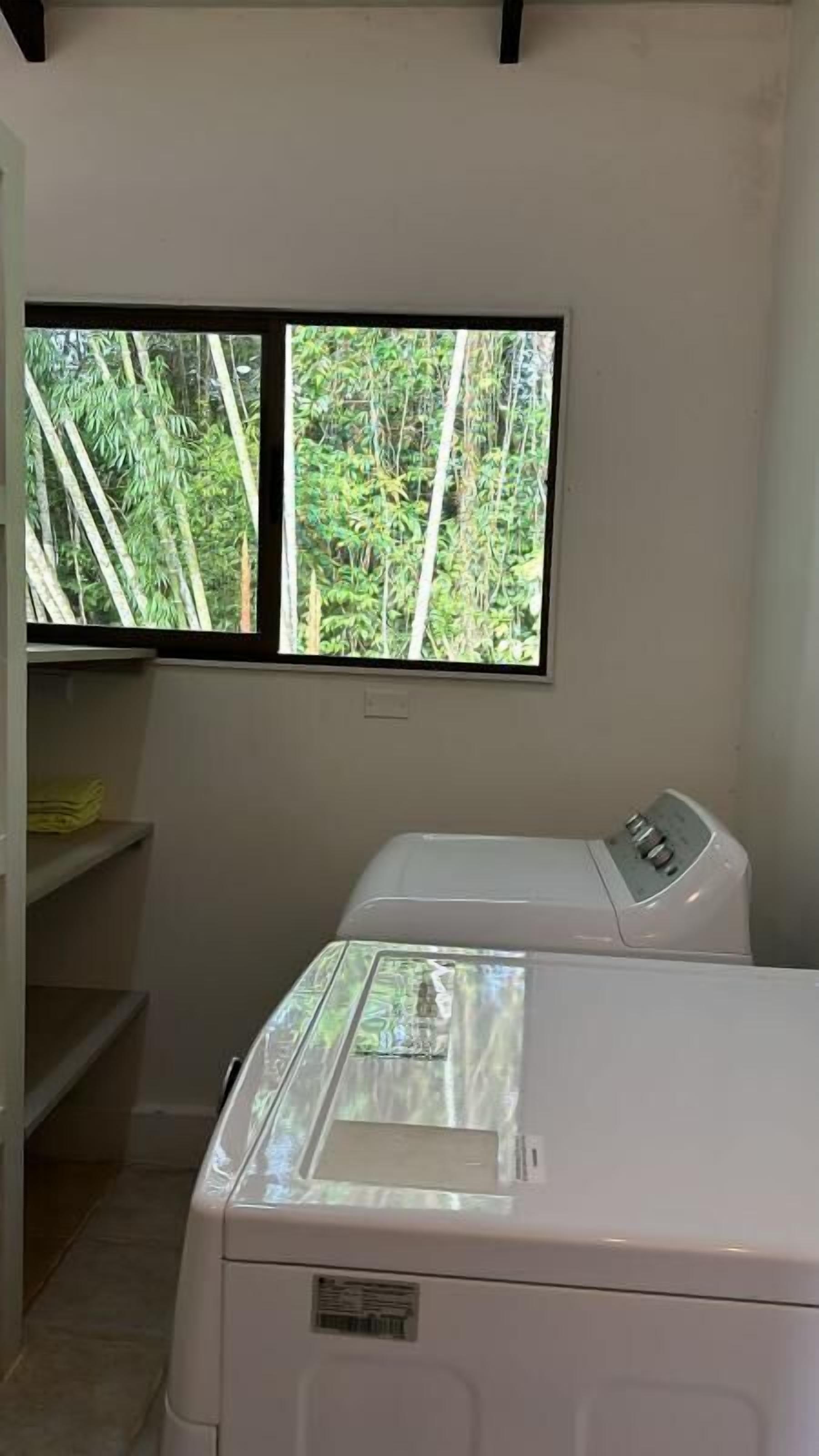 Uma lavanderia com duas máquinas de lavar e secar empilhadas, uma janela com vista para o verde e uma prateleira com toalhas dobradas.