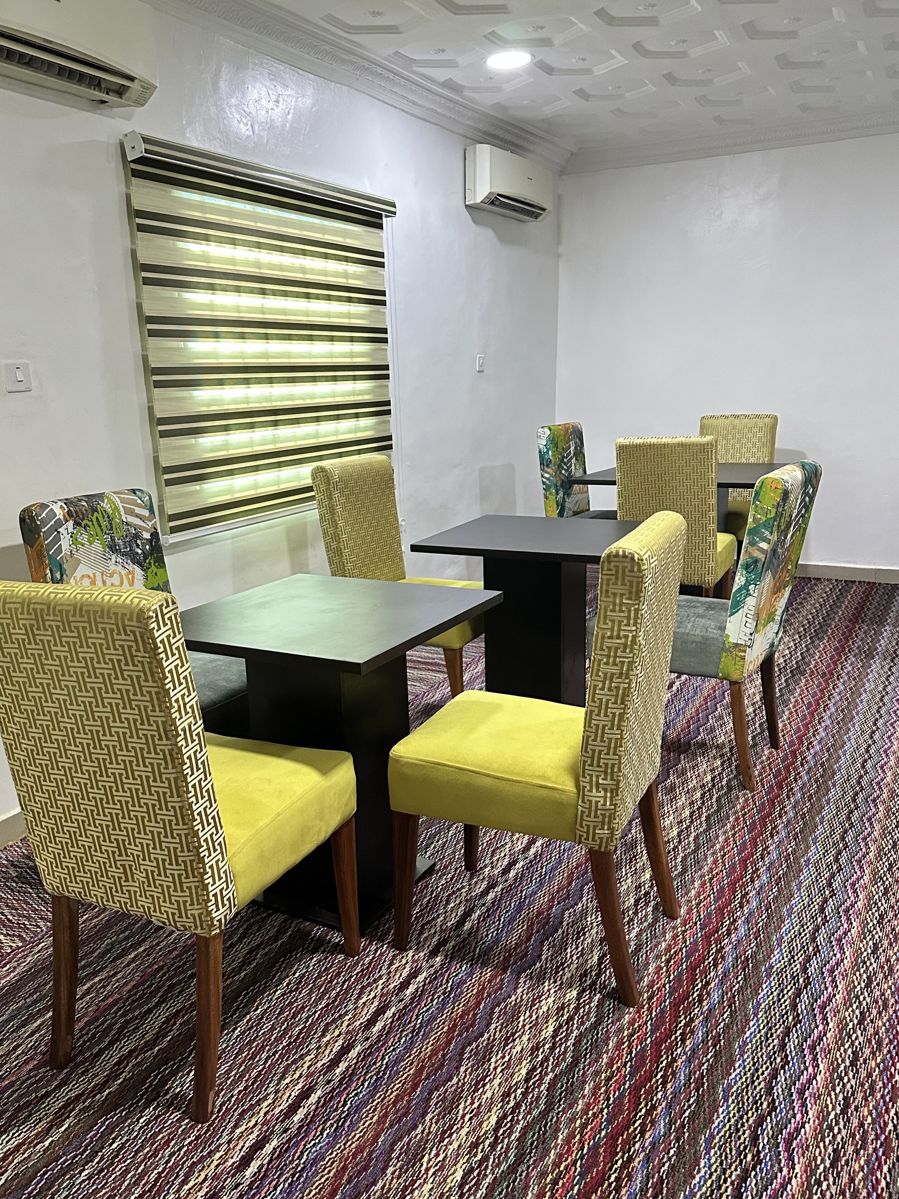 Uma sala de conferências com uma mesa preta, cadeiras amarelas e um tapete estampado.