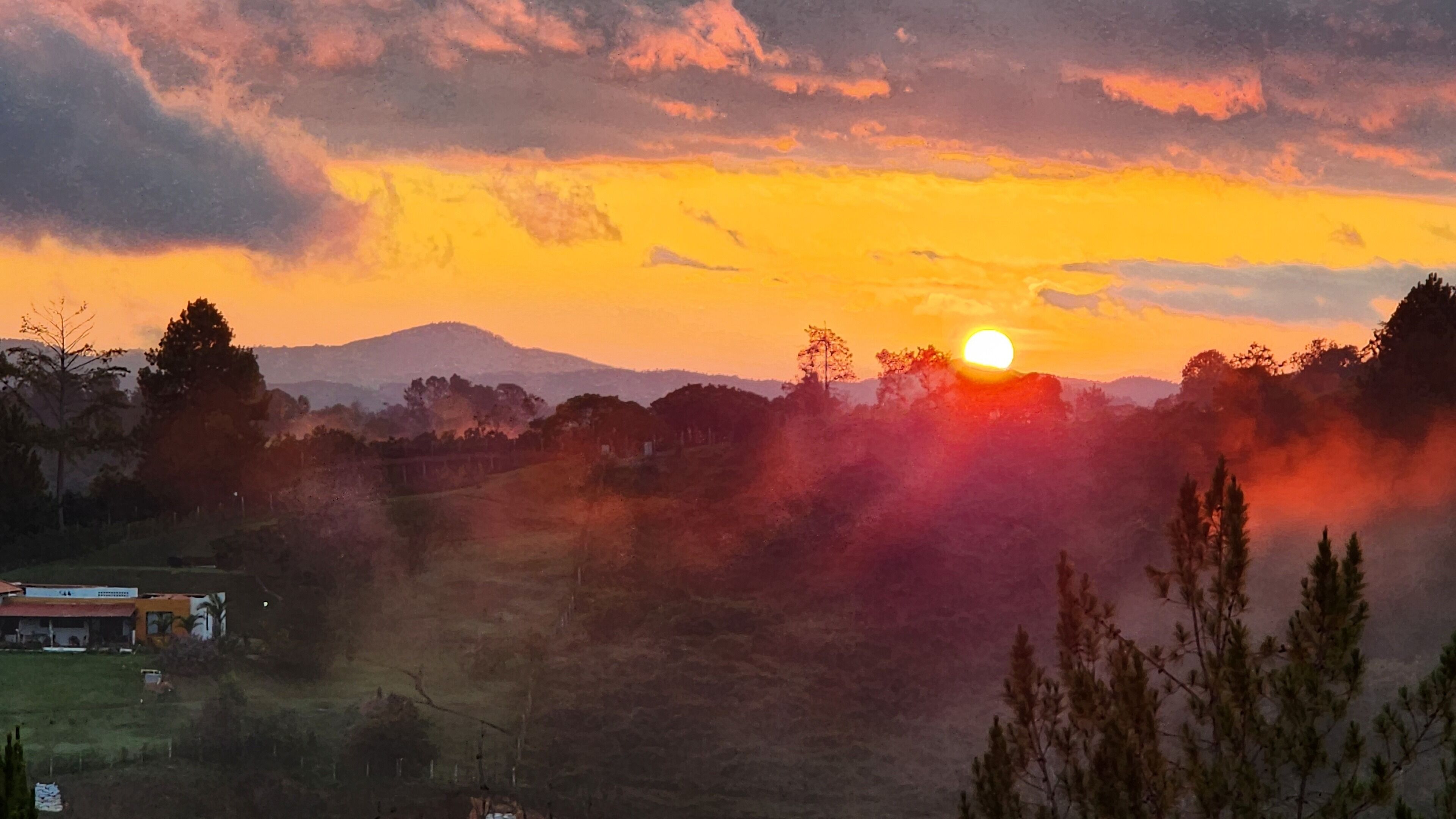 Pôr do sol sobre uma paisagem montanhosa, com um edifício em primeiro plano.