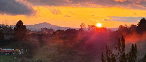 Pôr do sol sobre uma paisagem montanhosa, com um edifício em primeiro plano.