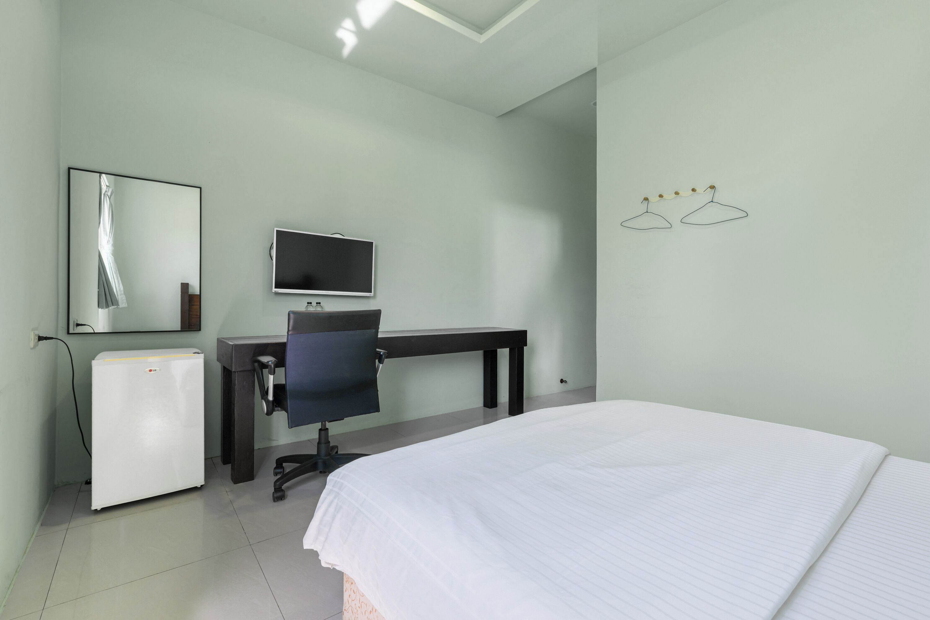 Quarto de hotel com uma cama, uma escrivaninha, uma cadeira, uma televisão e um pequeno frigorífico.