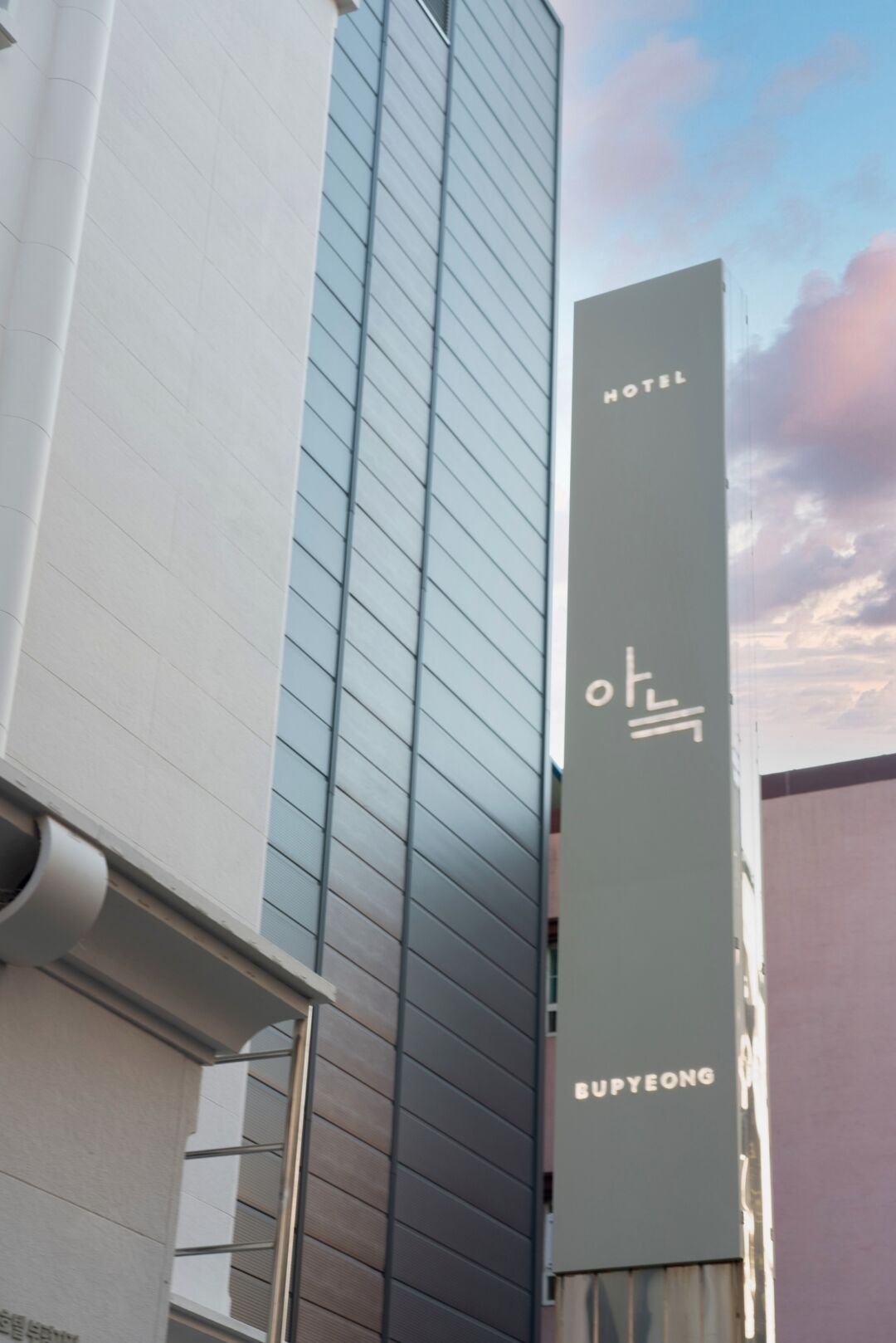 Um edifício de hotel moderno com uma placa vertical exibindo o nome 'BUPYEONG' e a palavra 'HOTEL' no topo.
