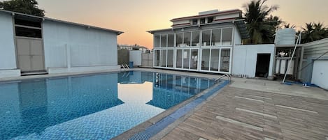 Piscina com deck ladrilhado, cercada por edifícios com amplas janelas e céu claro.