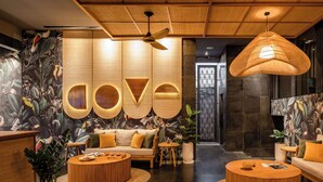 Um lobby moderno com área de estar central, parede decorativa com as letras 'LOVE' e uma planta grande.
