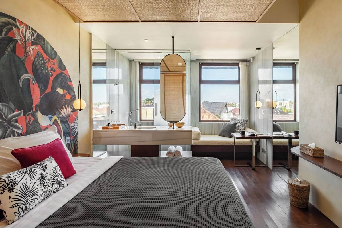 Quarto de hotel moderno com cama grande, escrivaninha, sofá e vista para a cidade.