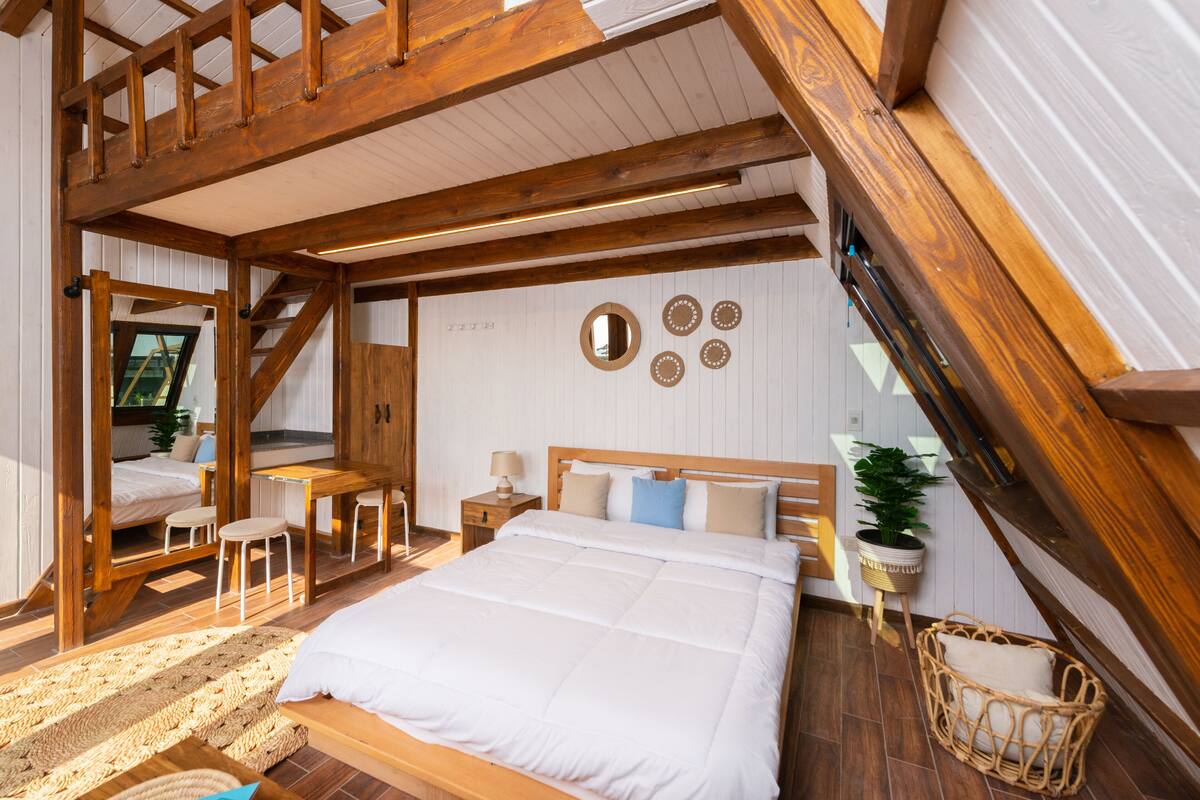 Quarto com uma cama grande, vigas de madeira, escrivaninha e uma cadeira.