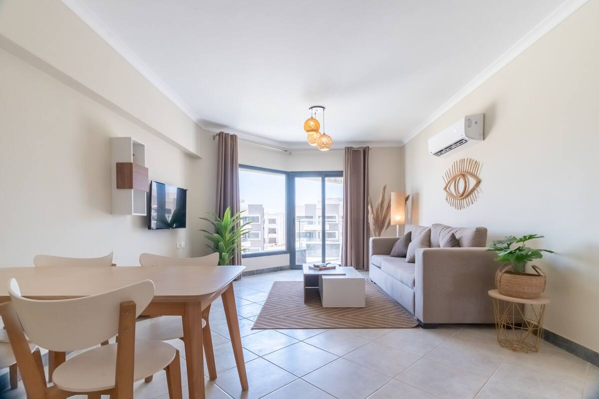 Uma sala de estar moderna com área de jantar, um sofá e uma TV fixada na parede.