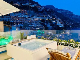 Terraço no telhado com hidromassagem, espreguiçadeira e vista para uma vila no campo ao entardecer.