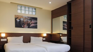 Quarto de hotel moderno com uma cama grande, uma mesa de cabeceira, uma luminária na parede, um espelho grande e uma janela com vidro decorativo.