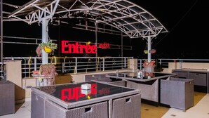 Uma área externa com mesas e cadeiras de vime e uma placa grande com a palavra 'Entree'.