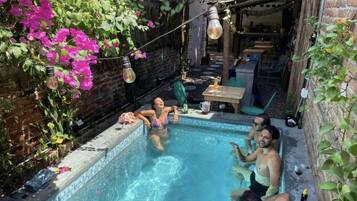 Piscina cercada por paredes de tijolo e vegetação, com uma mesa e cadeiras por perto.