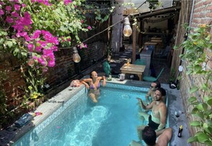 Piscina cercada por paredes de tijolo e vegetação, com uma mesa e cadeiras por perto.