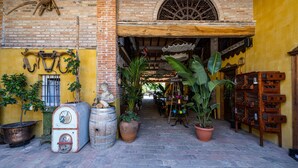 Um beco estreito com um edifício amarelo, plantas em vasos e um barril de madeira.