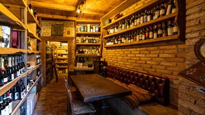 Um bar acolhedor com prateleiras de madeira repletas de garrafas, uma mesa comprida e um assento de couro.