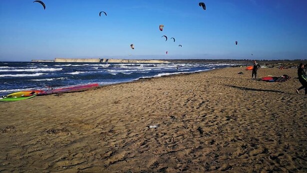 Uma praia com pessoas empinando pipas e alguns caiaques coloridos na areia.