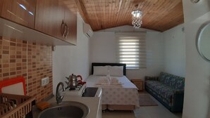 Quarto compacto com cama, pequena cozinha, pia e janela com persianas.