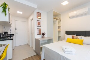 Quarto de hotel moderno com cama, escrivaninha, cozinha compacta e closet espaçoso.