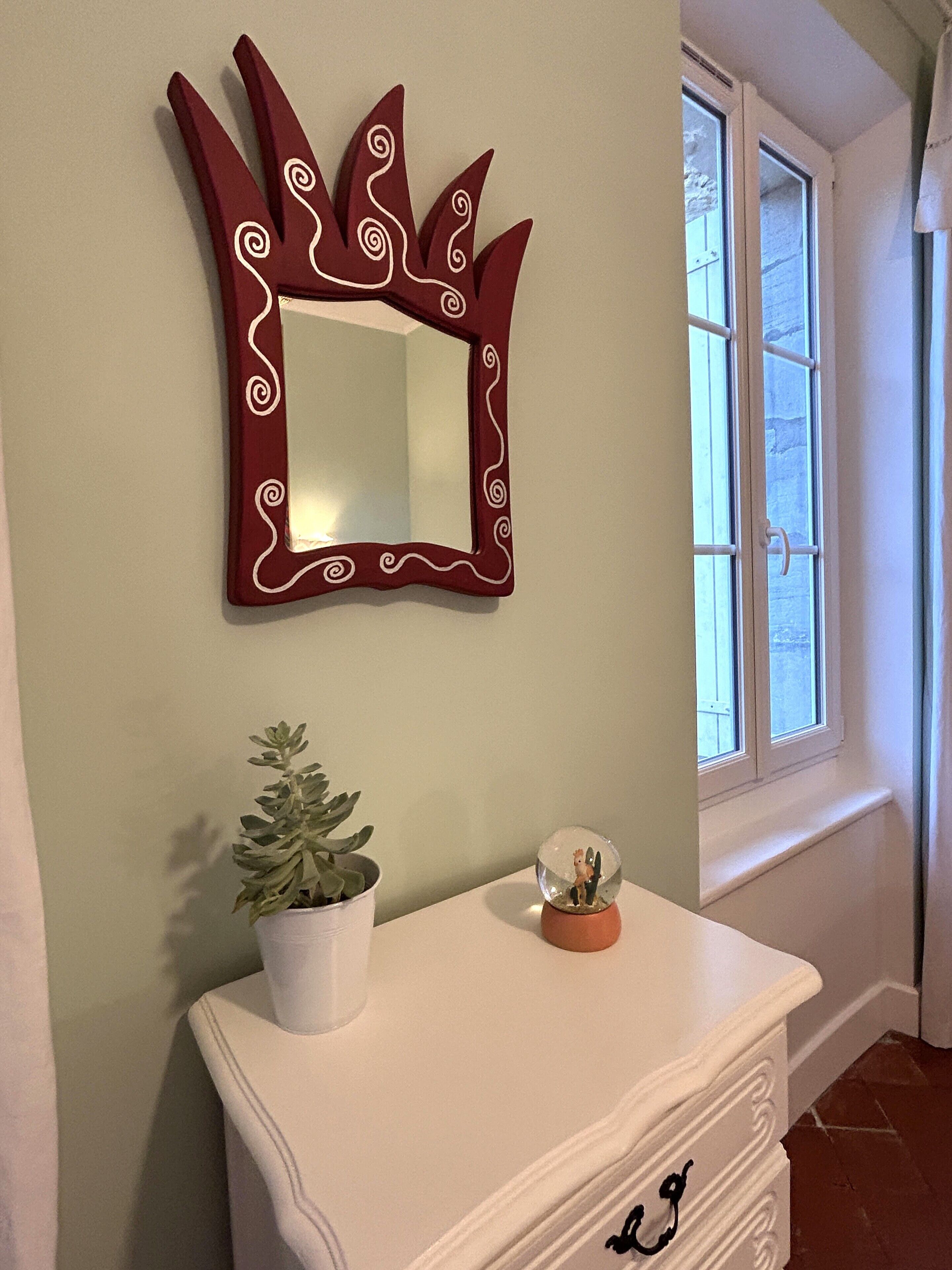 Uma cômoda branca com espelho e uma pequena planta em vaso.