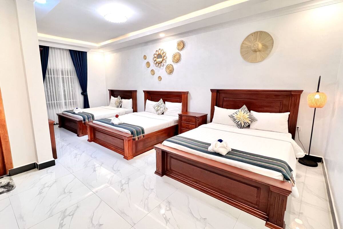 Quarto de hotel com duas camas de madeira, piso de mármore, um espelho grande e um objeto decorativo na parede.