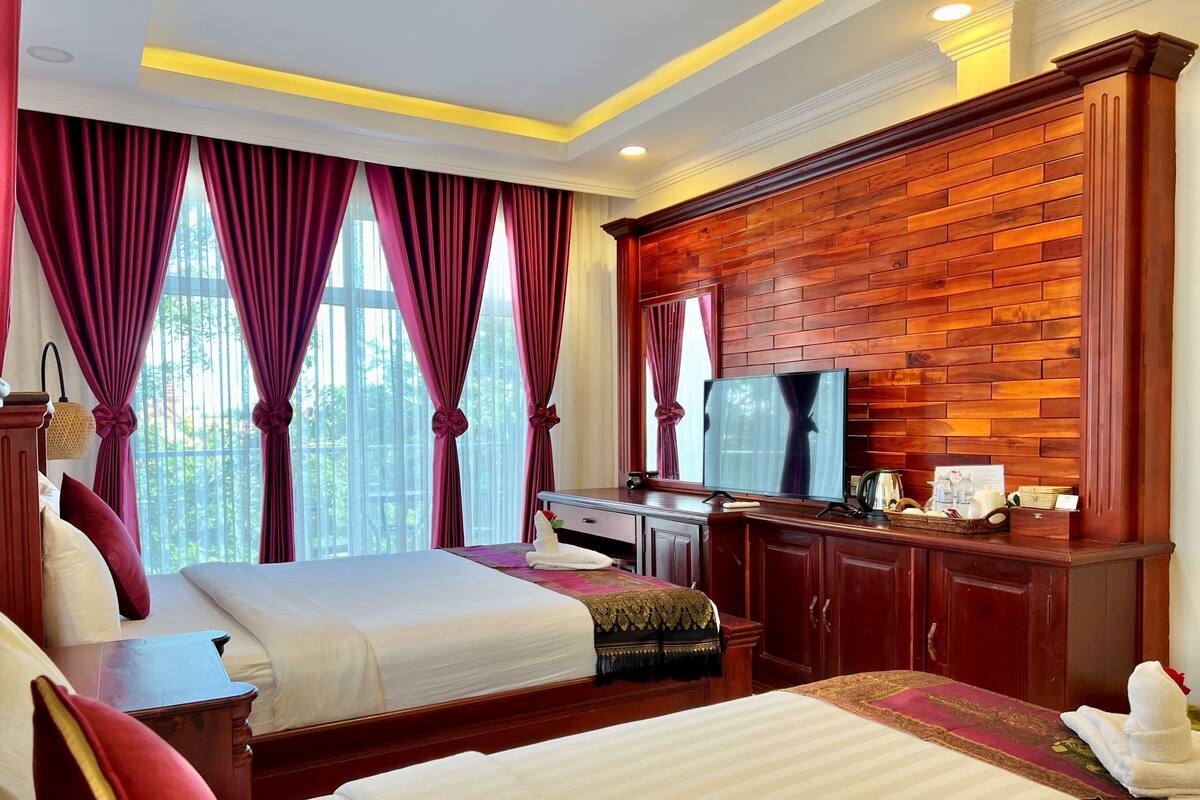 Quarto de hotel com duas camas, televisão, secretária com computador e parede com padrão de tijolos.
