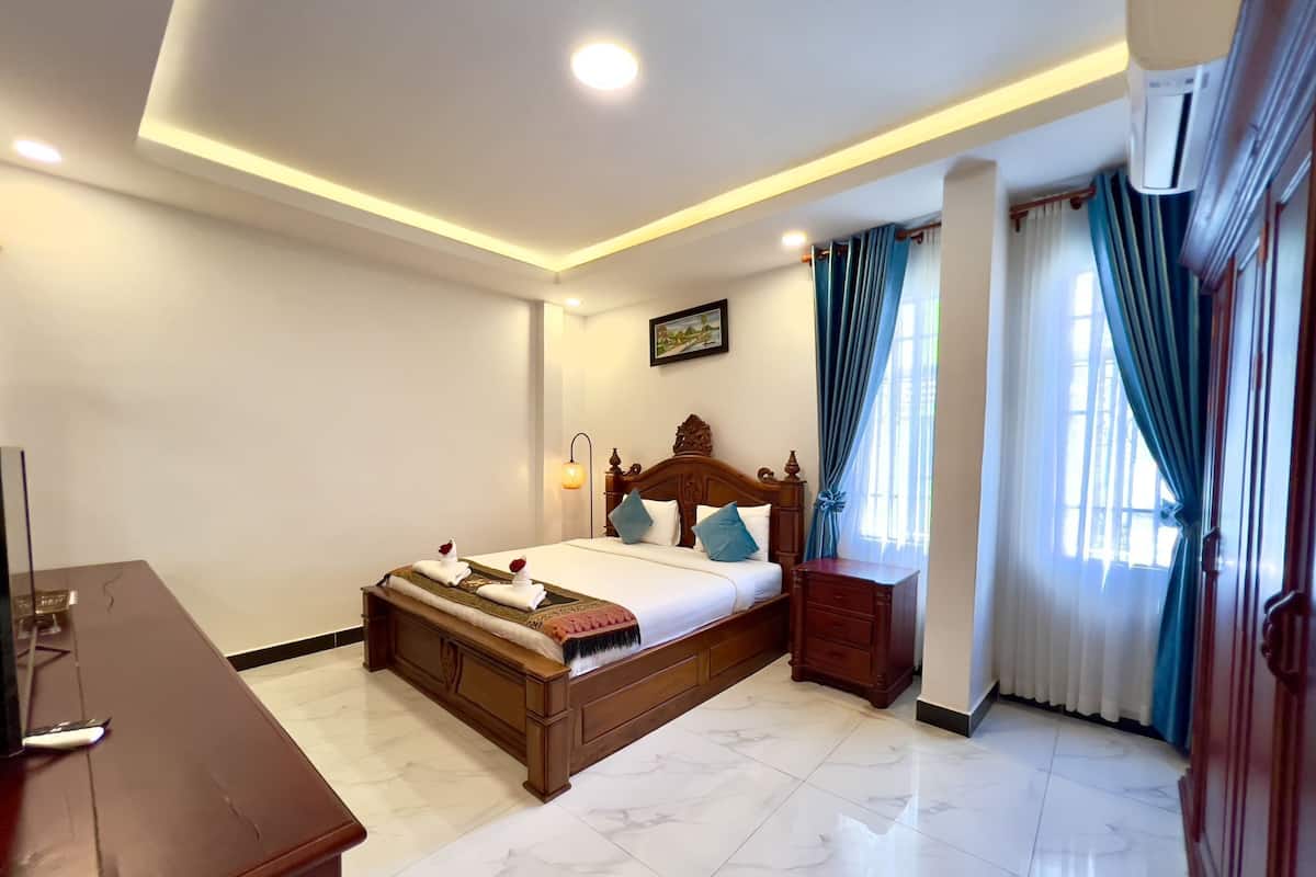 Quarto de hotel com uma cama grande, mesas de cabeceira, cômoda de madeira e luminária no teto.