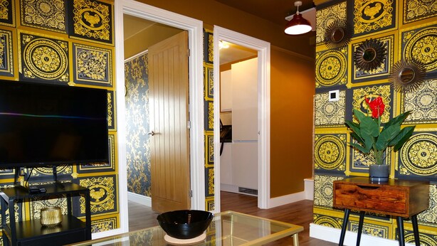 Uma sala de estar com uma mesa de centro de vidro, uma TV de tela plana, uma mesa lateral de madeira e um vaso decorativo com flores.