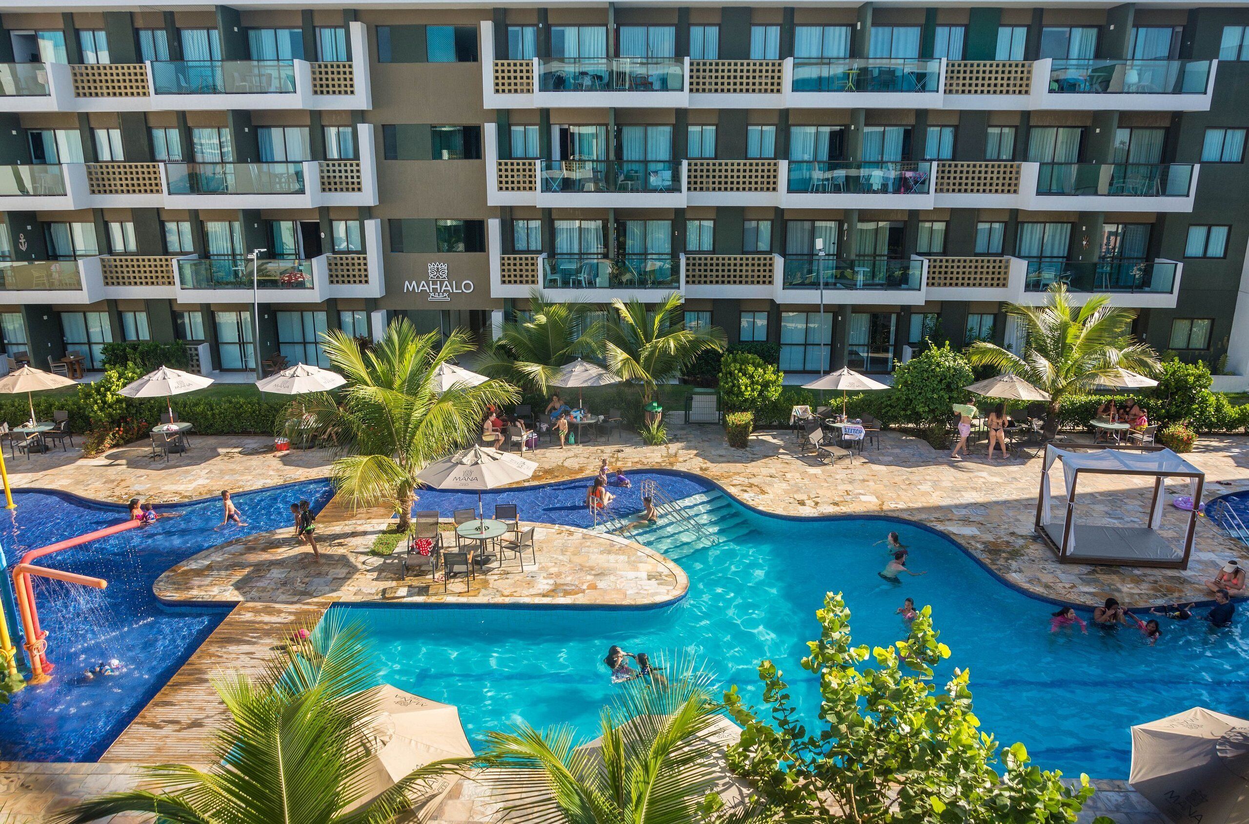 Um hotel com piscina, área de estar externa e palmeiras.