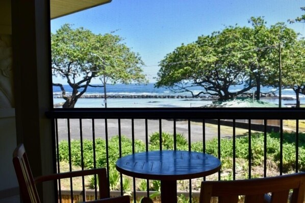 Uma varanda com vista para o oceano, uma mesa redonda e duas cadeiras.