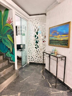 Um corredor com porta de vidro, parede branca decorativa, quadro emoldurado e mesa consola com planta.
