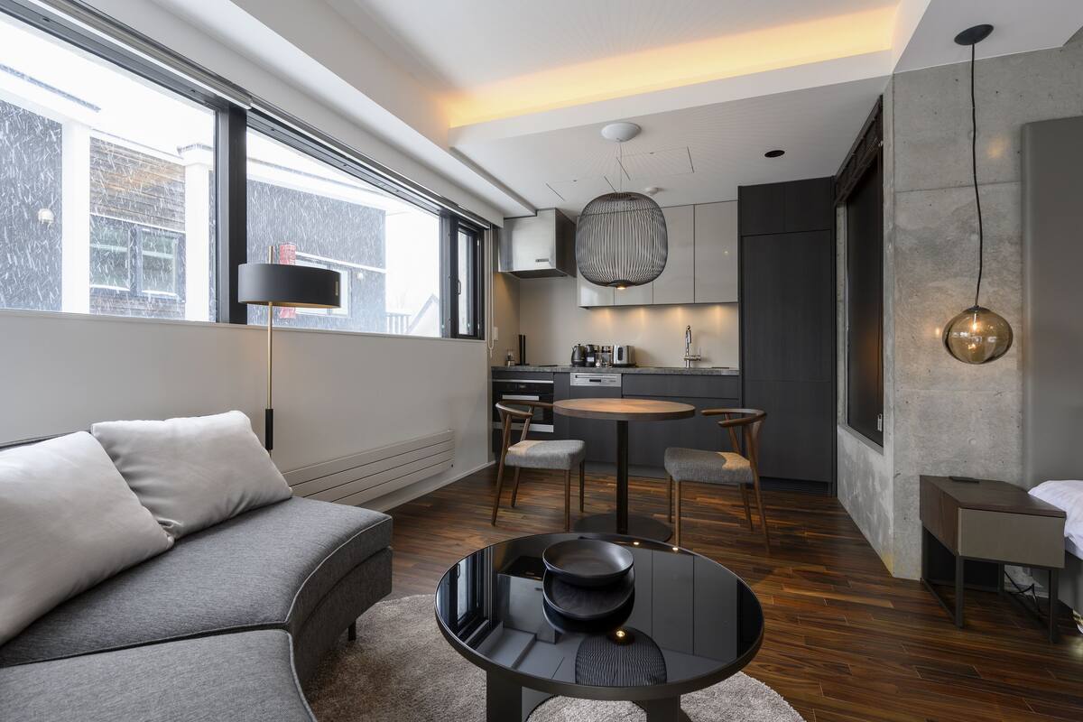 Uma sala de estar moderna com um sofá cinzento, uma mesa de centro redonda e uma área de jantar com uma mesa e cadeiras redondas.