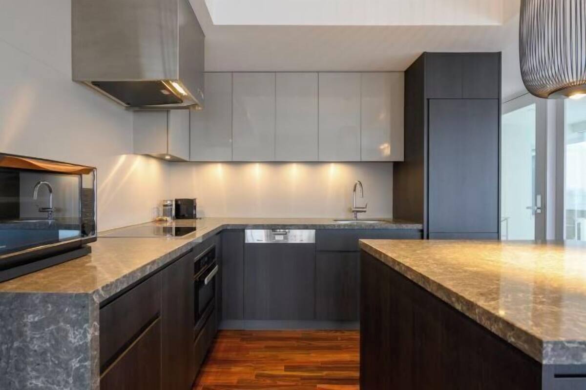 Uma cozinha moderna com armários escuros, lava-louças embutida e piso de madeira.