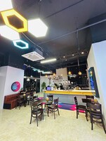 Um restaurante moderno com luminárias hexagonais no teto, um balcão central e várias áreas de estar.