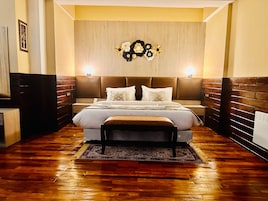 Quarto com piso de madeira, cama com roupa de cama branca, duas luminárias de cabeceira e um objeto decorativo na parede acima da cama.