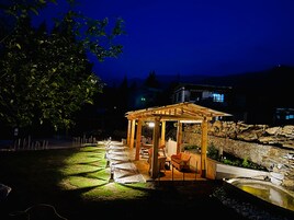 Um gazebo com parede de pedra e um pequeno lago, cercado por um caminho de pedra e cadeiras.